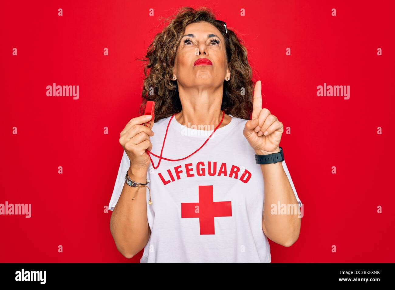 Middle age senior summer lifeguard woman holding whistle over red ...