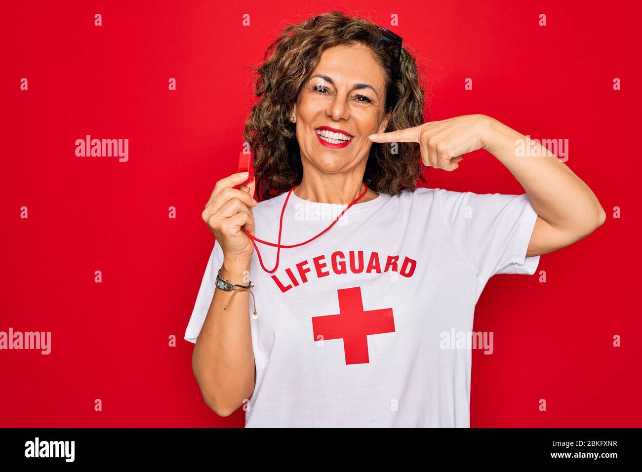 Middle age senior summer lifeguard woman holding whistle over red ...