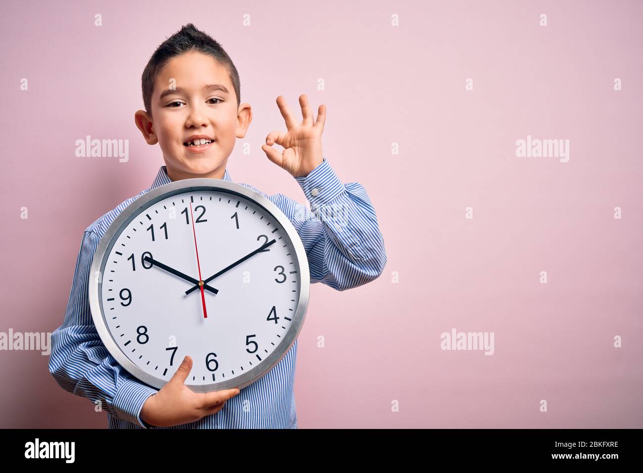 Young little boy kid holding big minute clock over isolated pink ...