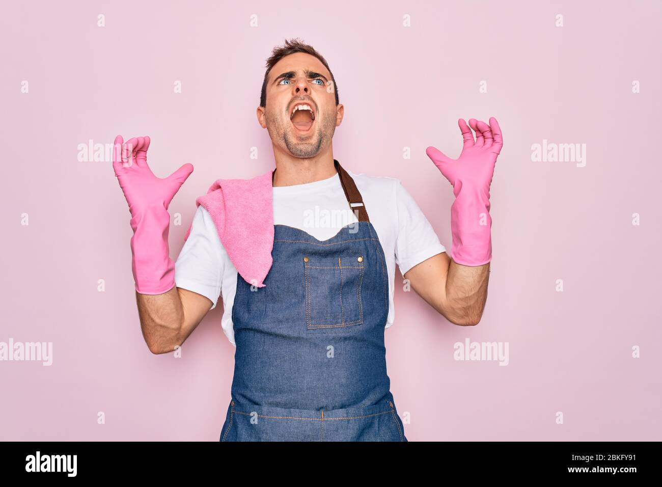 Young cleaner man with blue eyes cleaning wearing apron and gloves over ...