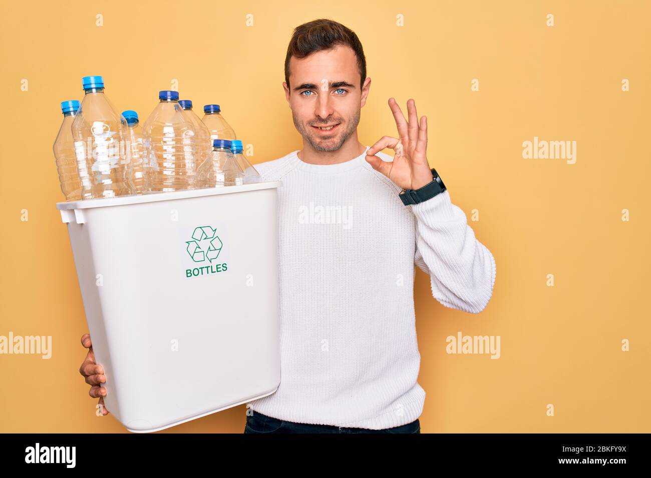 Young handsome man with blue eyes recycling holding wastebasket with ...