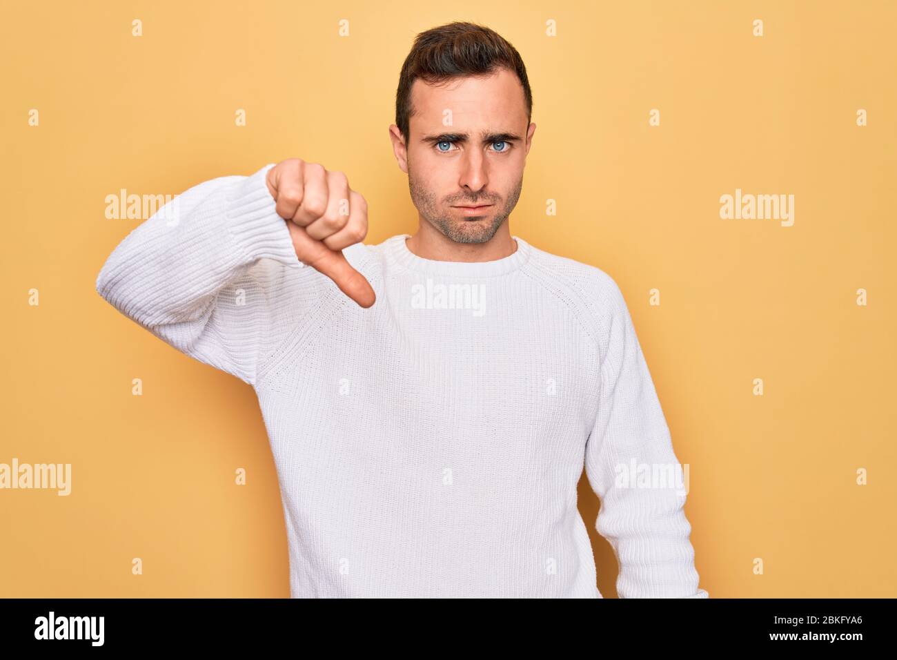 Young handsome man with blue eyes wearing casual sweater standing over ...