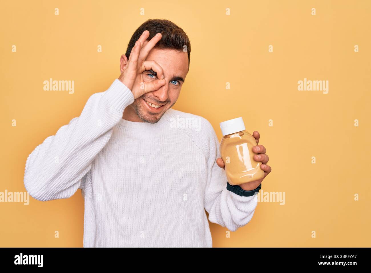 Young handsome man holding bottle of mustard sauce condiment over ...
