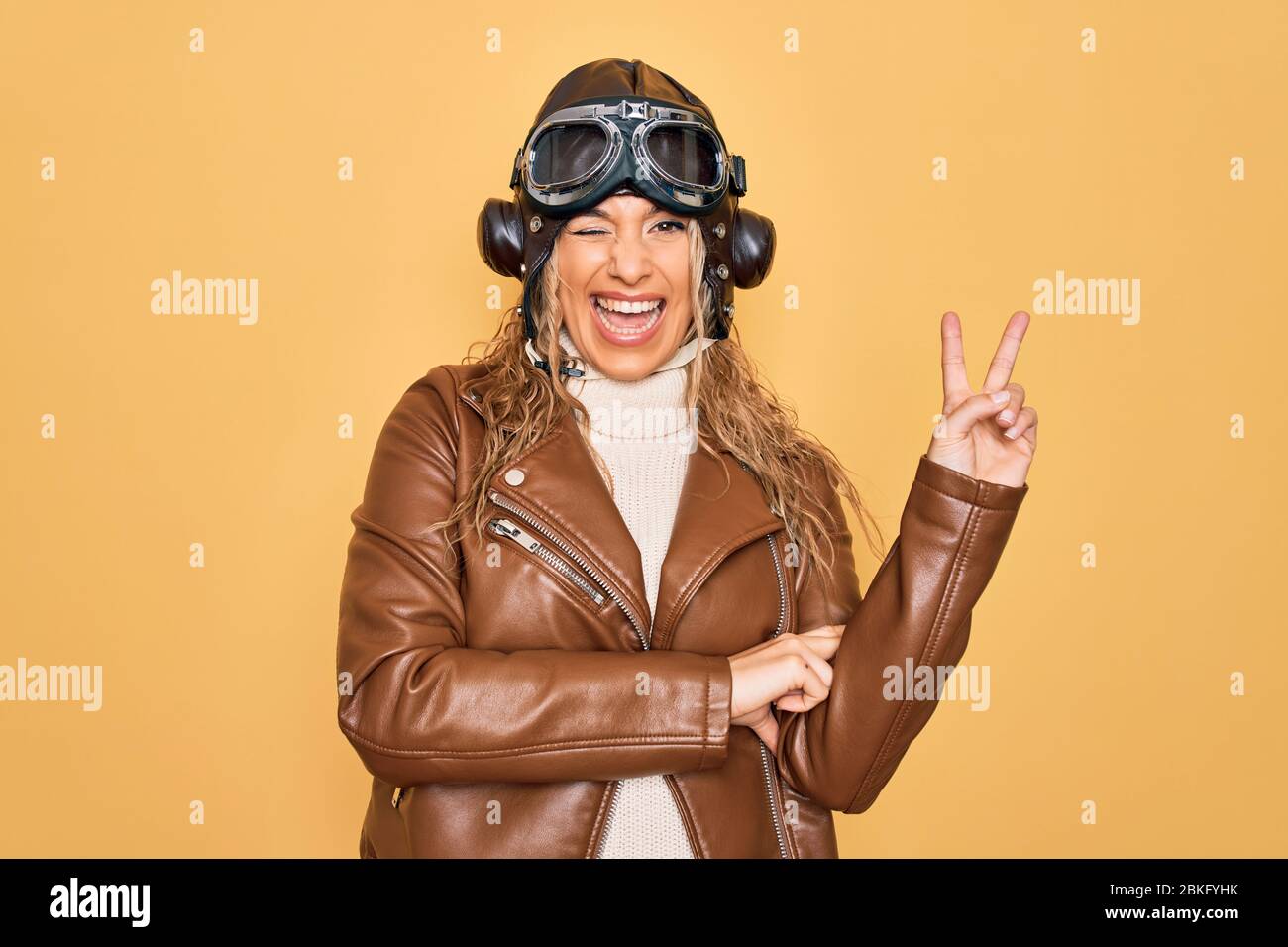 Young beautiful blonde aviator woman wearing vintage pilot helmet whit ...