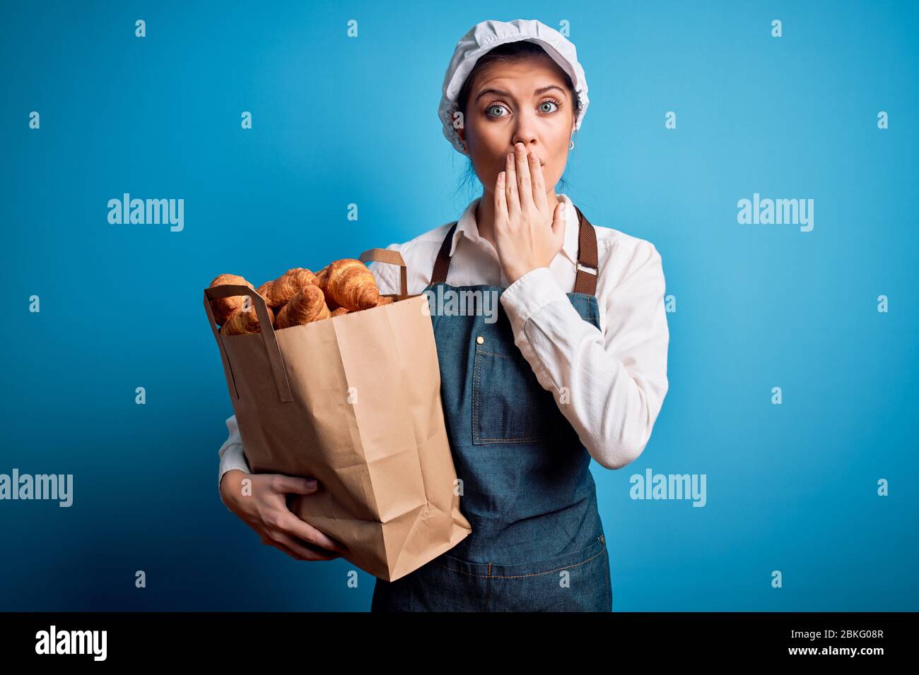 Young beautiful baker woman with blue eyes wearing apron holding paper ...