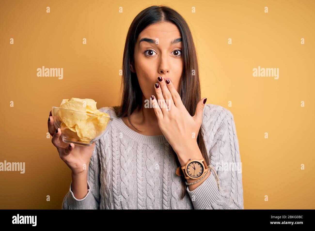 Young beautiful brunette woman holding bowl with snack potato chips ...