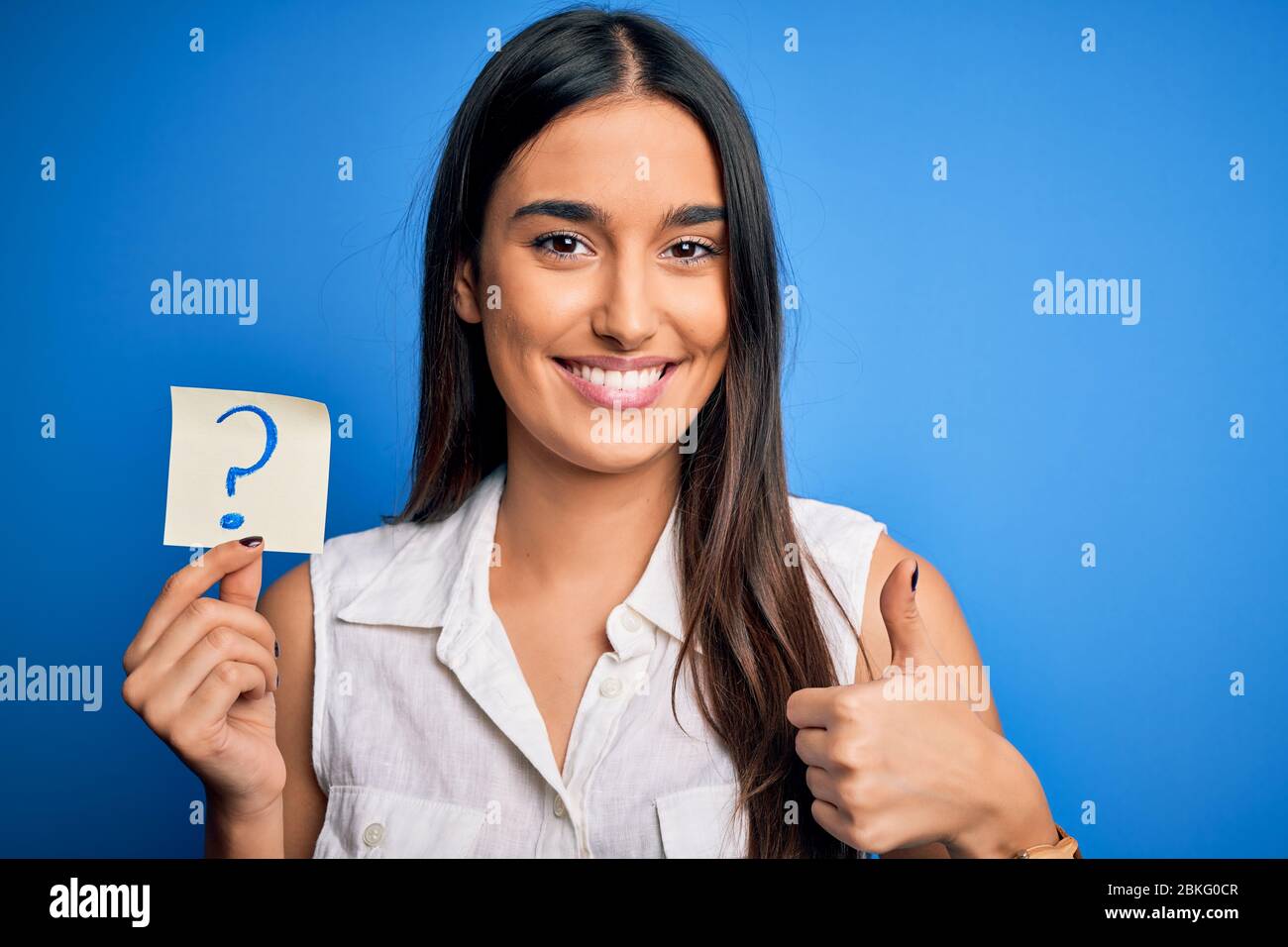 Young beautiful brunette woman holding paper with question mark symbol ...