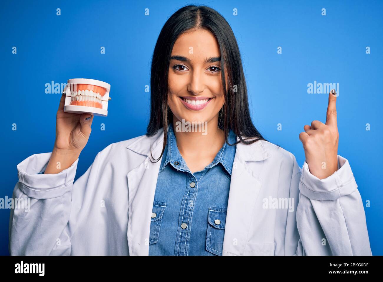 Young beautiful brunette dentist woman wearing coat holding plastic ...