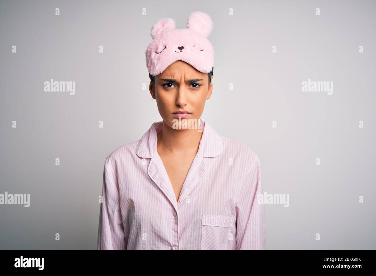 Young beautiful brunette woman wearing pajama and sleep mask over white ...