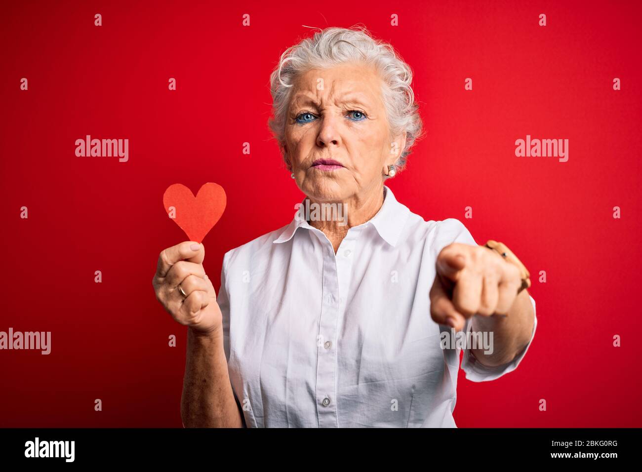 Senior beautiful woman holding paper heart standing over isolated red ...