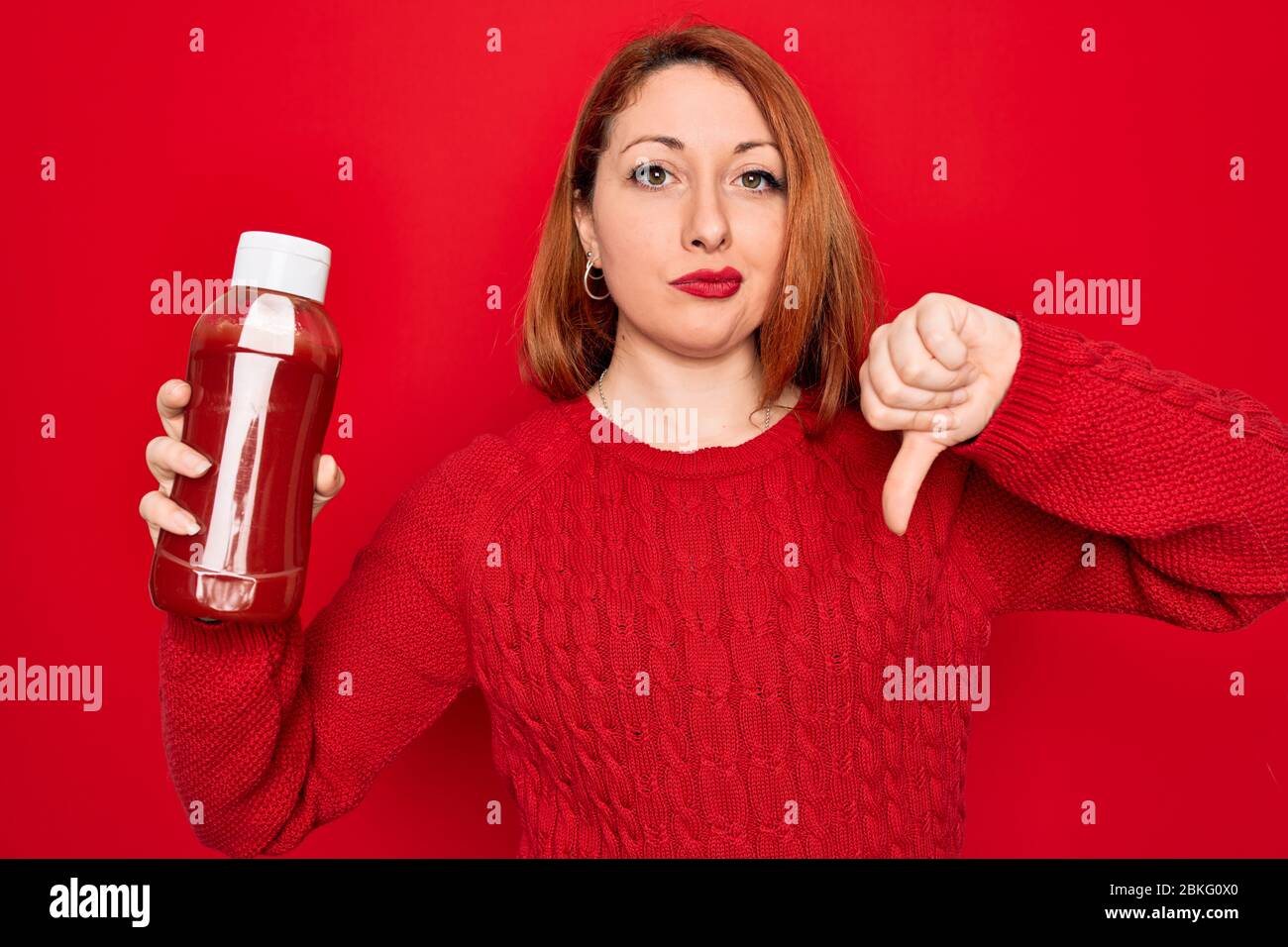 Beautiful redhead woman holding bottle of ketchup sauce condiment over ...