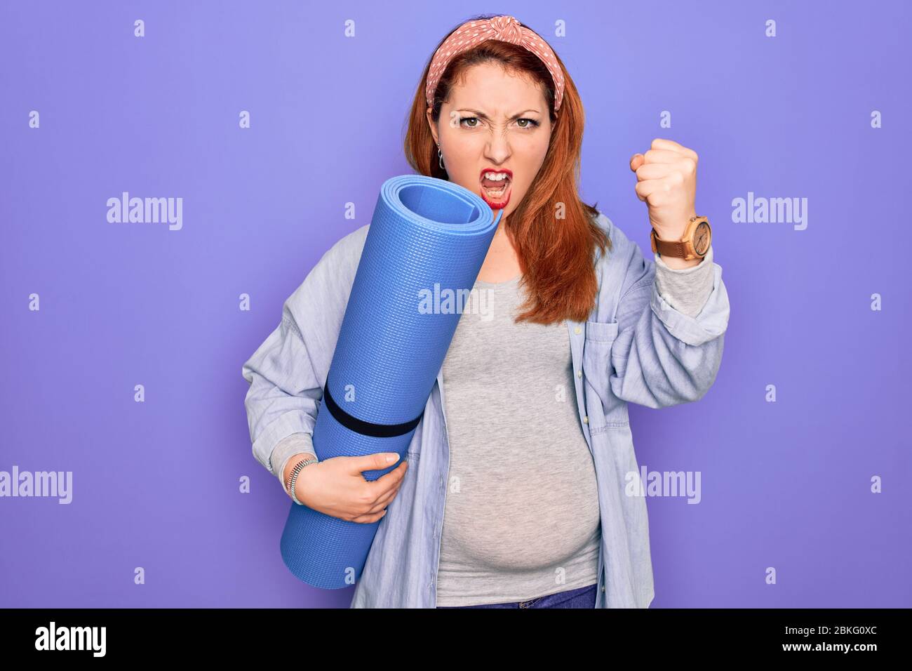 Young beautiful redhead pregnant woman expecting baby holding mat to do ...