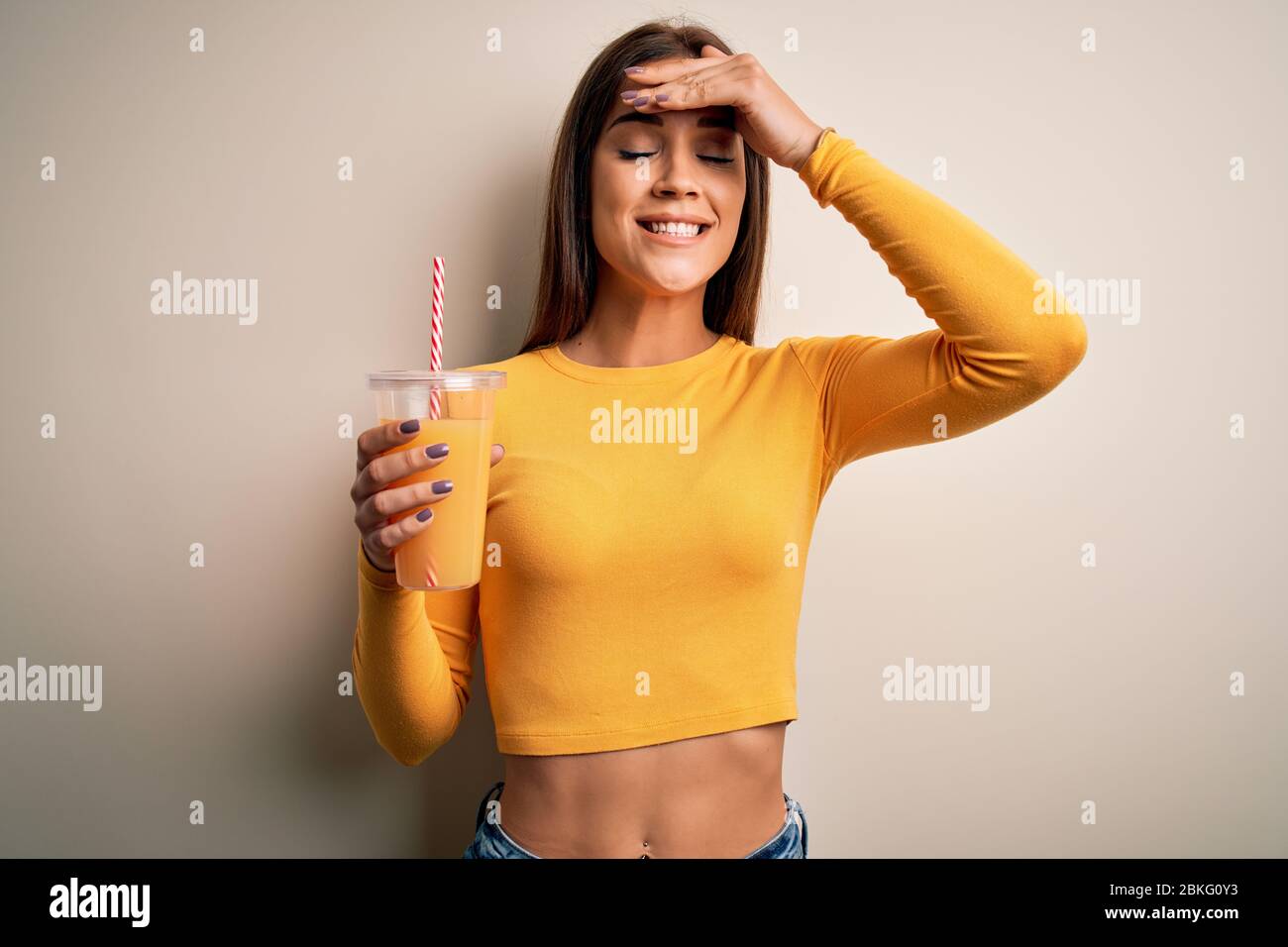 Young beautiful brunette woman drinking healthy orange juice over white ...