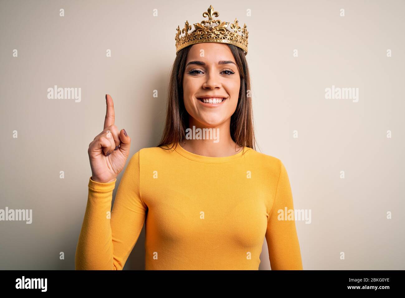 Young beautiful brunette woman wearing golden queen crown over white ...