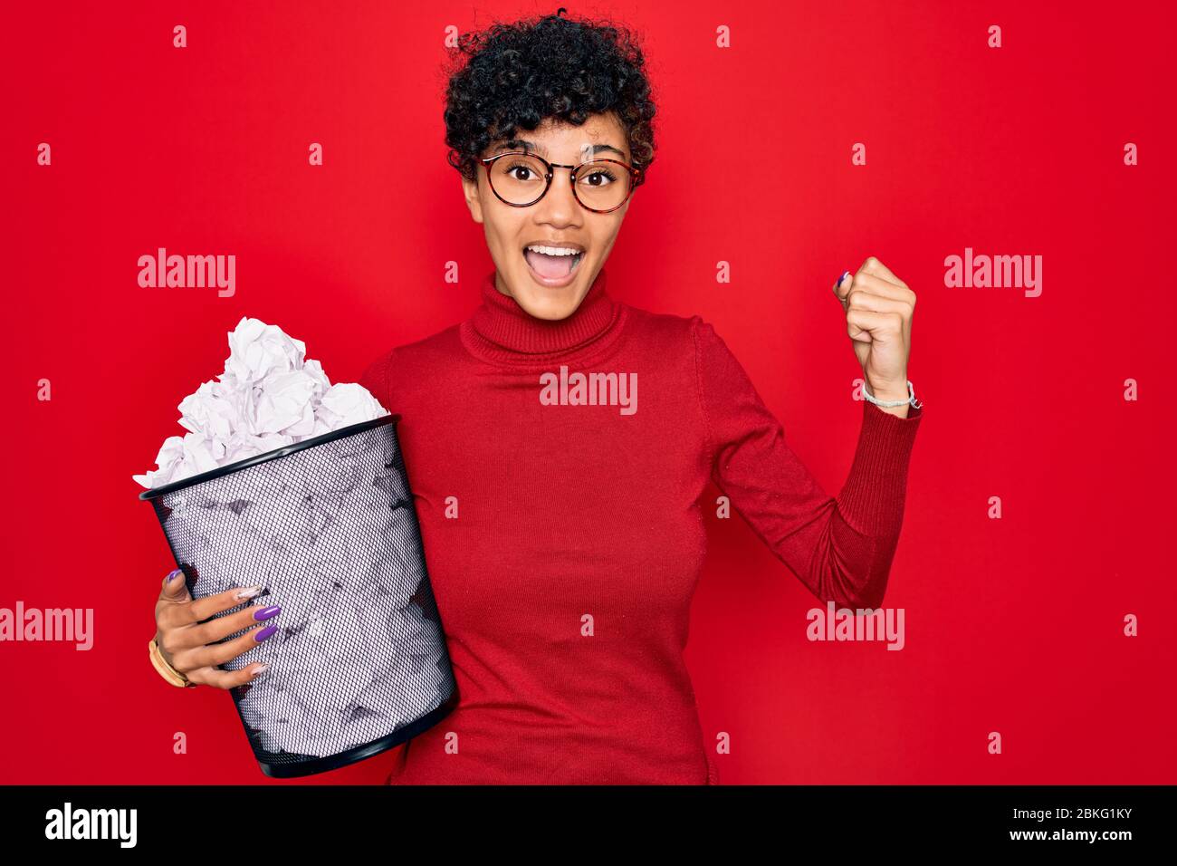 Young beautiful african american afro woman holding full paper bin with ...
