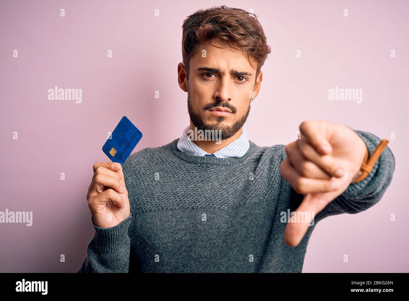 Young customer man with beard holding credit card for payment over pink ...