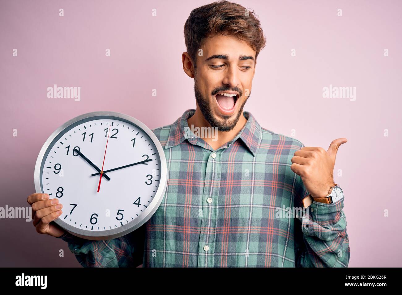 Young man with beard doing countdown using big clock over isolated pink ...