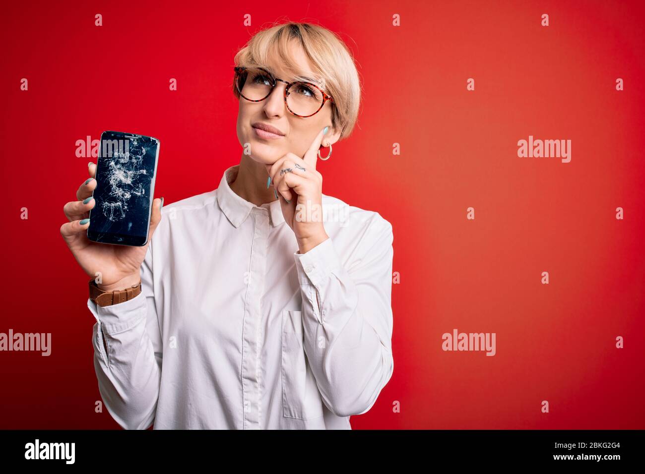 Young blonde woman with short hair holding broken smartphone over red ...