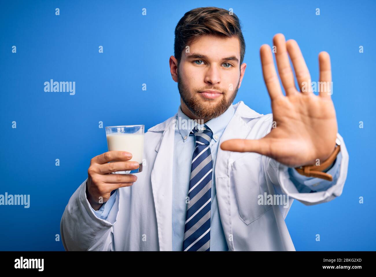 Young blond doctor man with beard and blue eyes wearing coat drinking ...