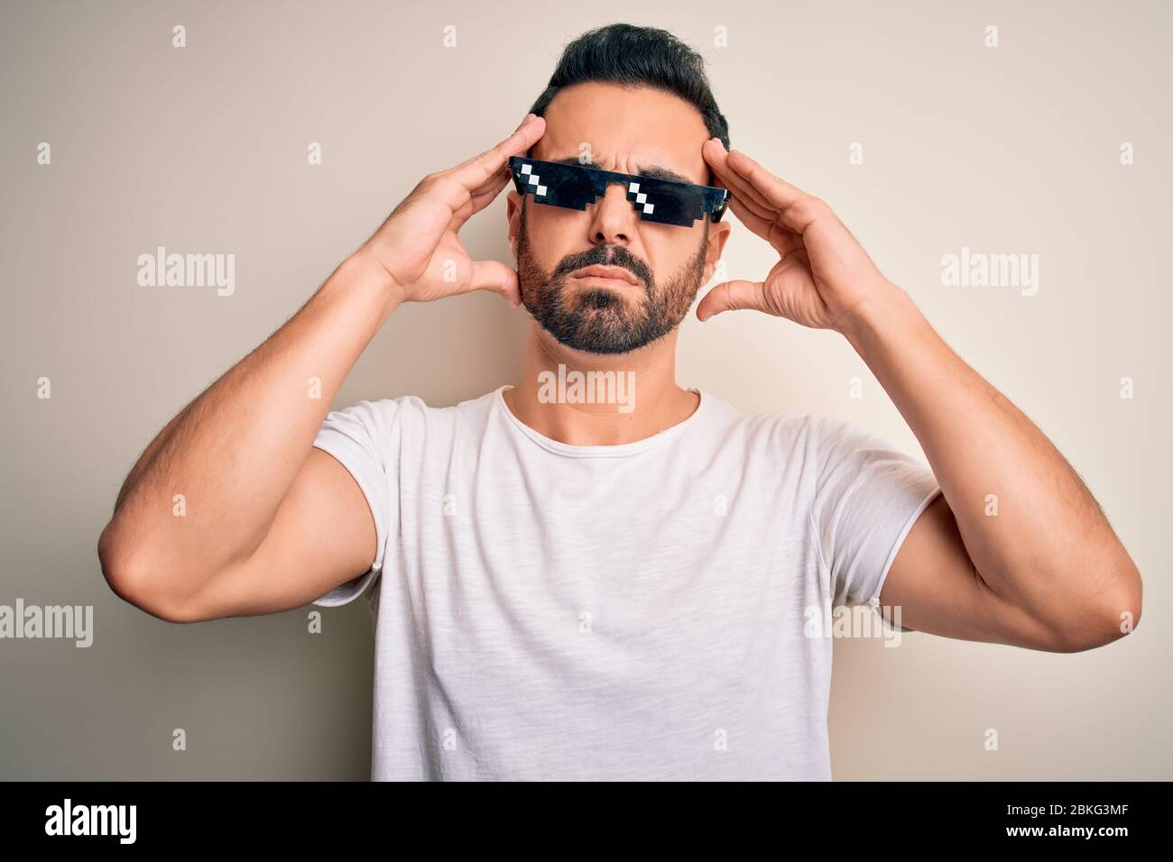 Young handsome man with beard wearing funny thug life sunglasses over ...