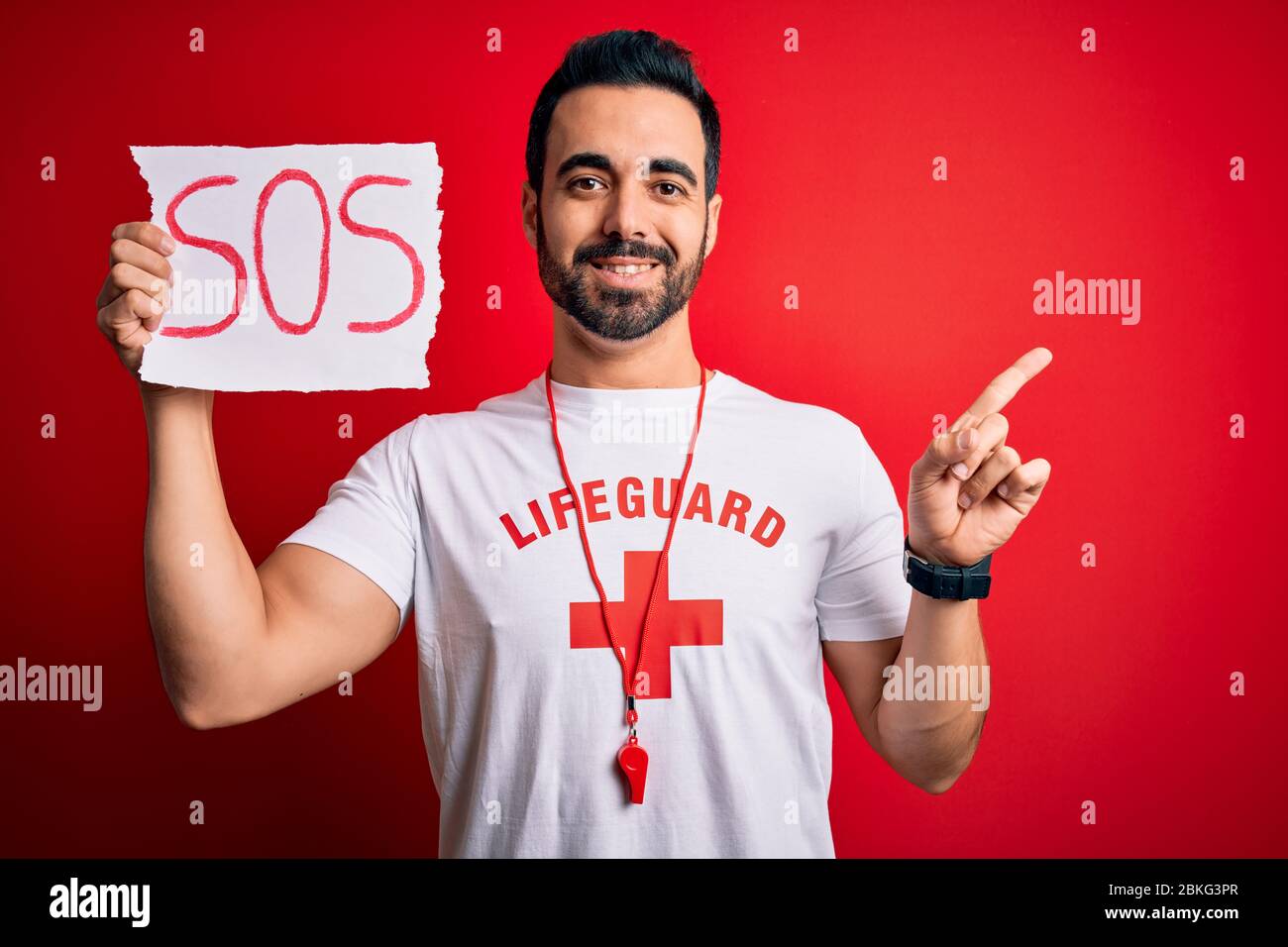 Young handsome lifeguard man with beard wearing whistle holding sos ...