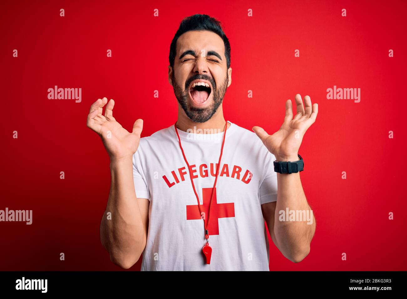 Young handsome lifeguard man with beard wearing whistle over isolated ...