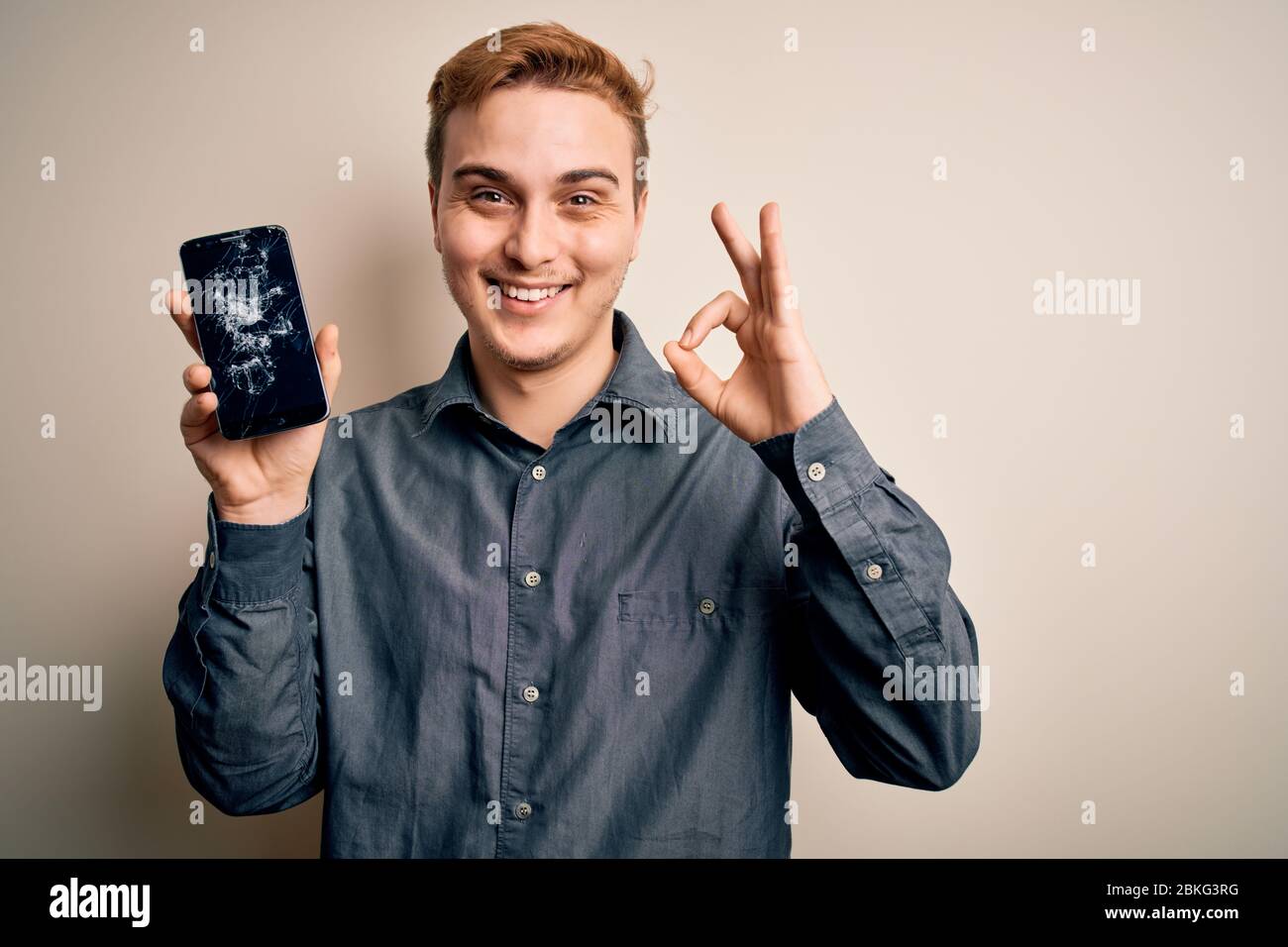Young handsome redhead man holding broken smartphone showing cracked ...