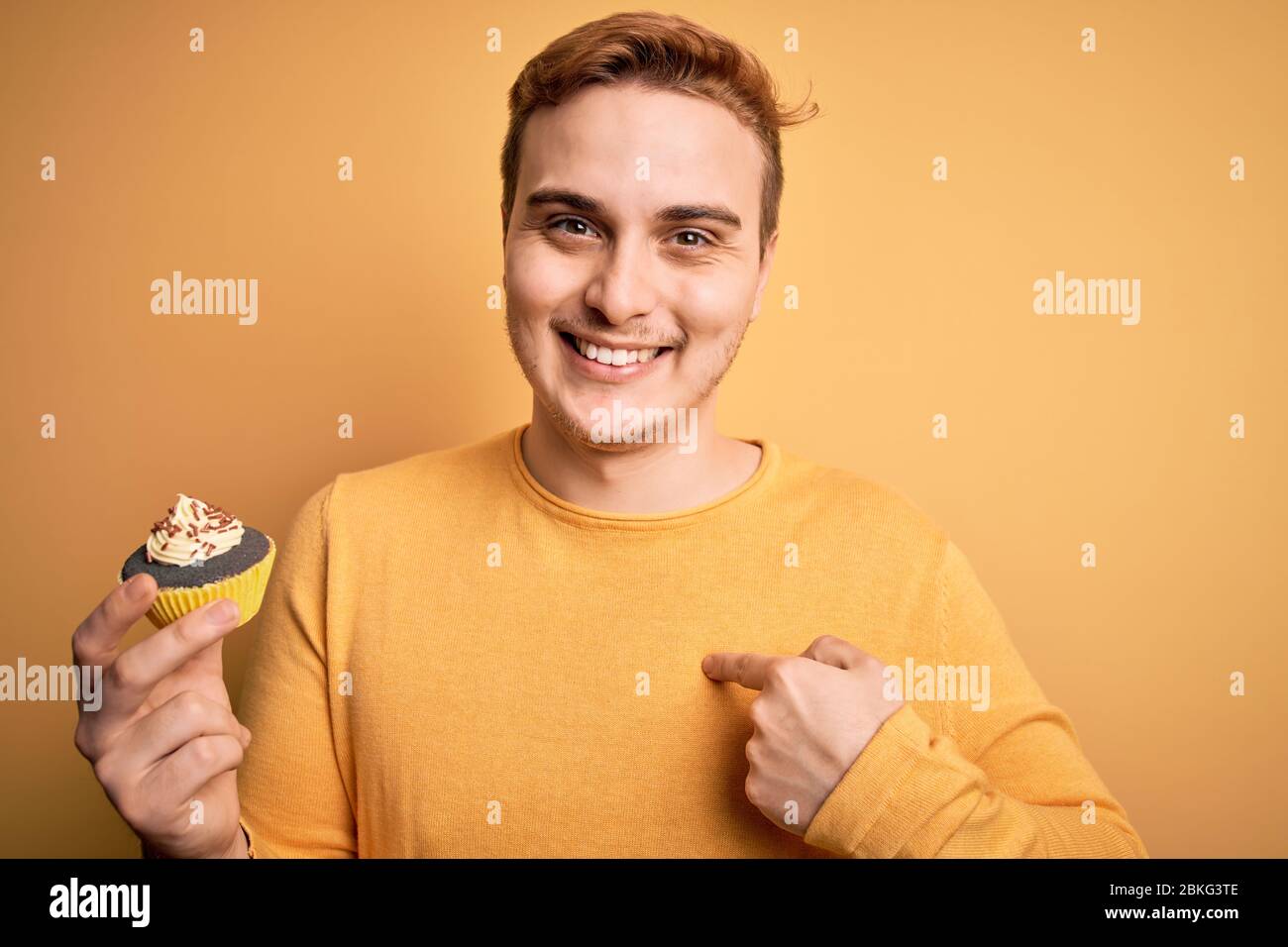 Young handsome redhead man eating sweet chocolate cupcake dessert over ...