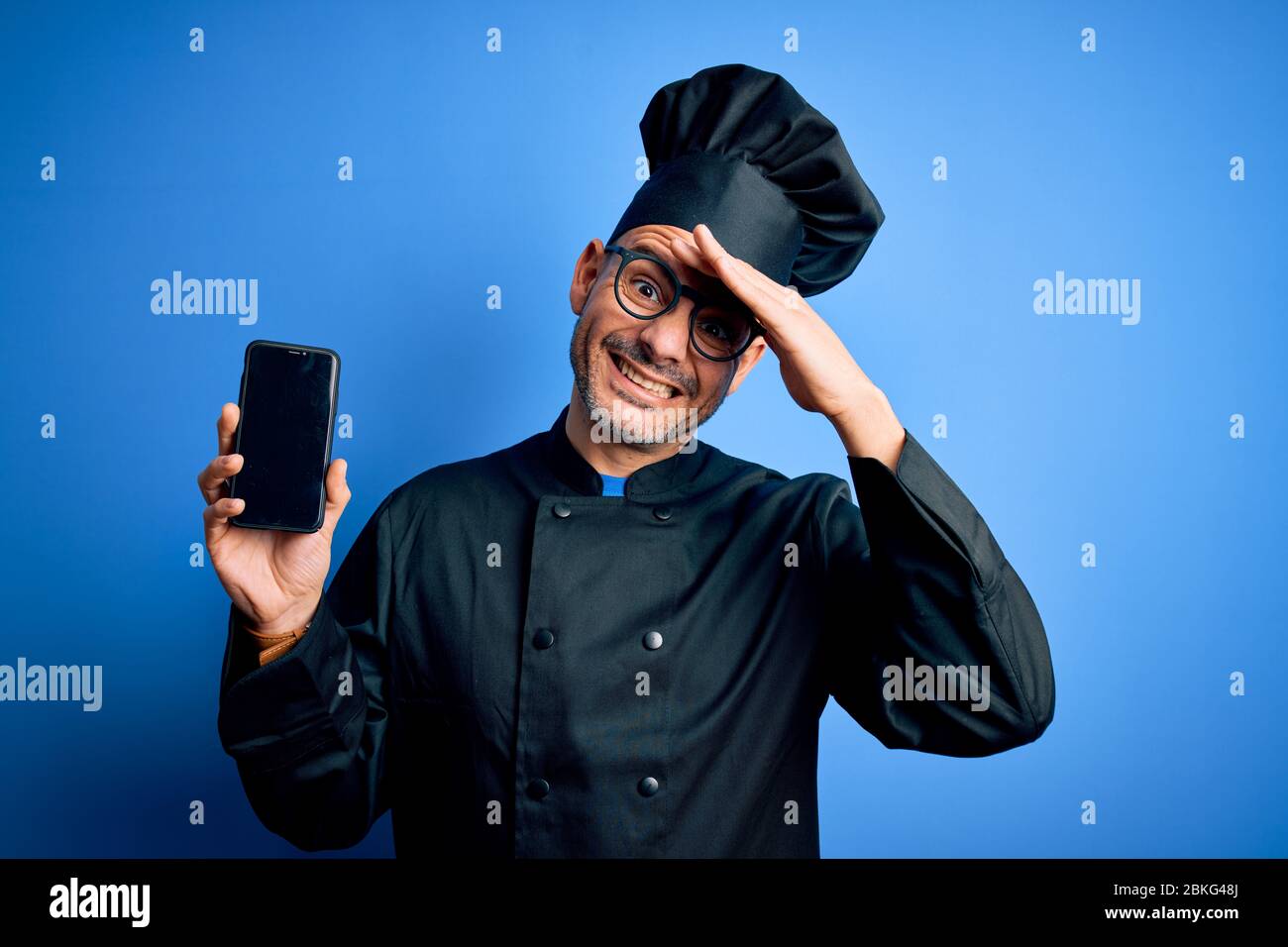 Young handsome chef man wearing uniform and hat holding smartphone over ...