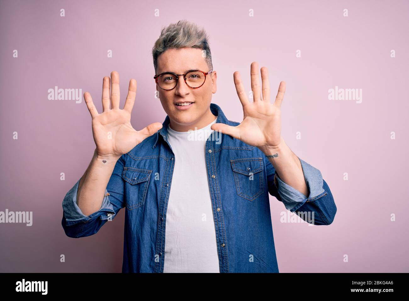 Young handsome modern man wearing glasses and denim jacket over pink ...