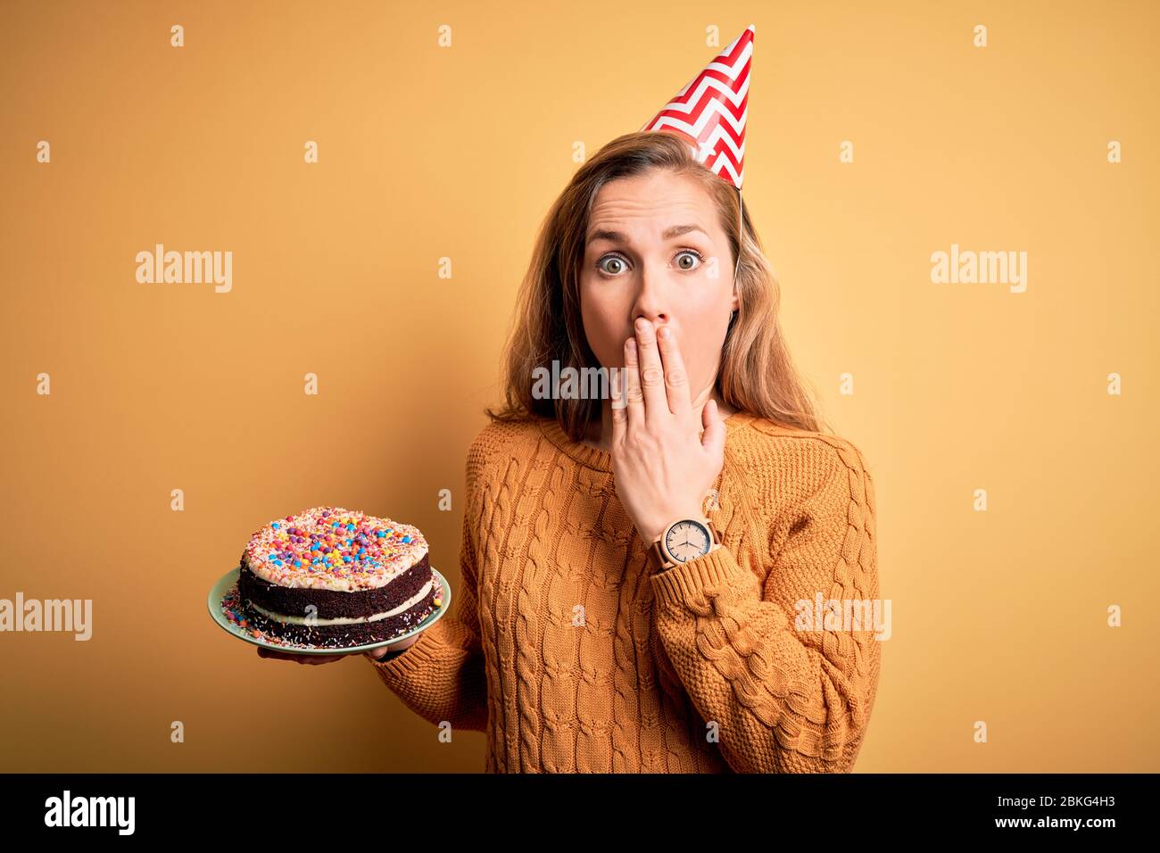 Young beautiful blonde woman holding birthday cake over isolated yellow ...