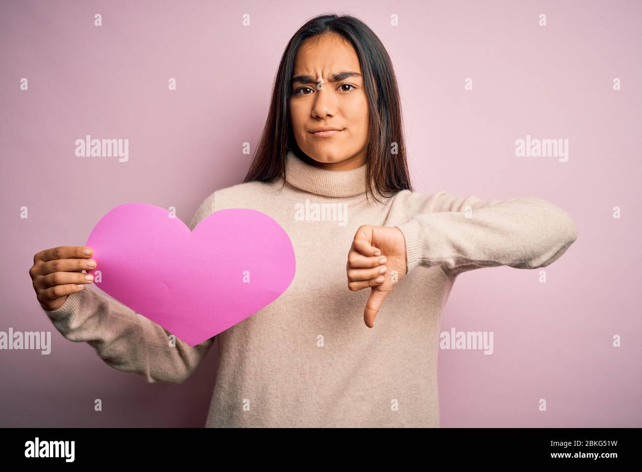 Young beautiful asian woman holding pink heart standing over isolated ...