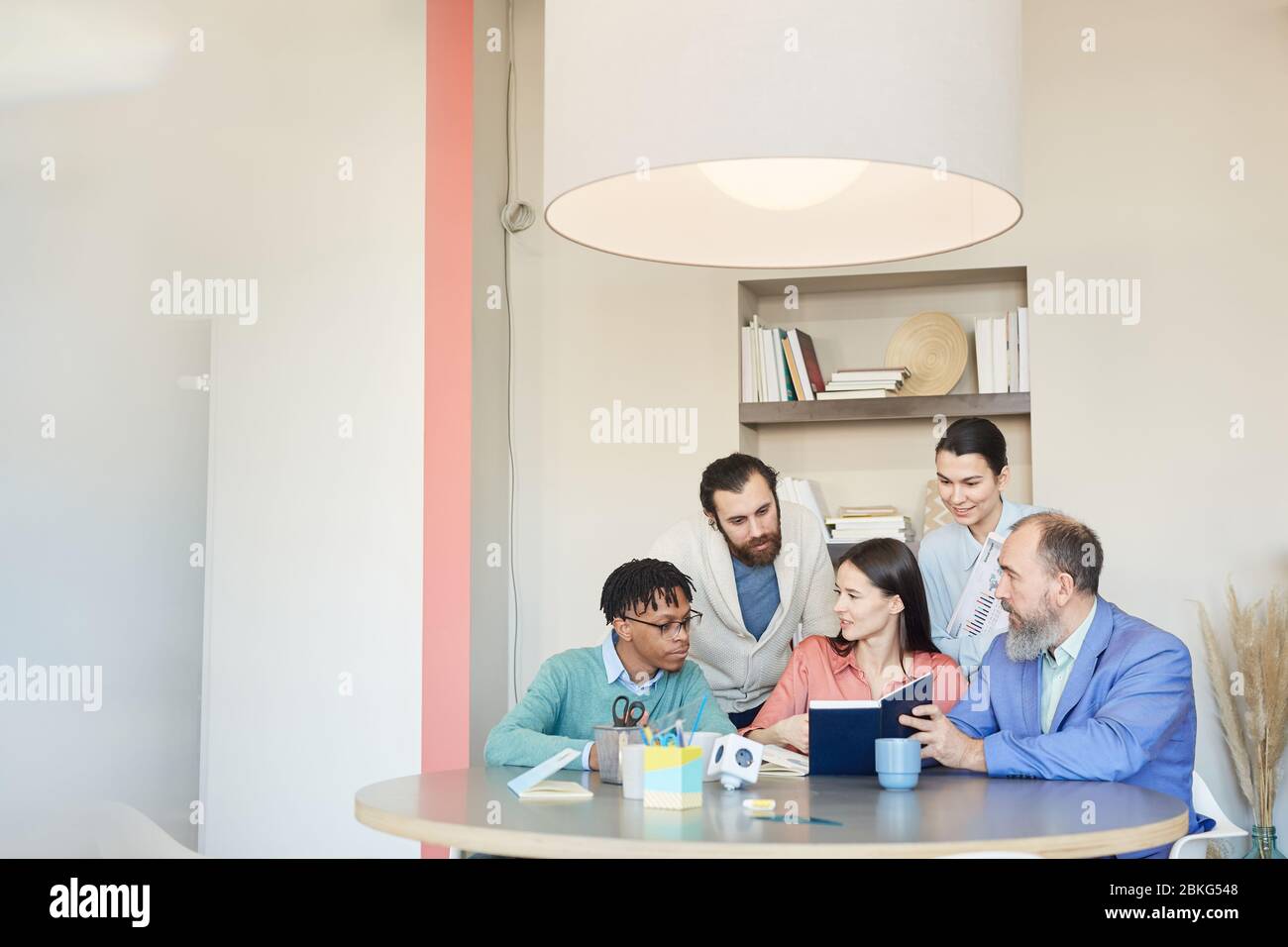 Group of five modern office workers gathered together discussing issues ...