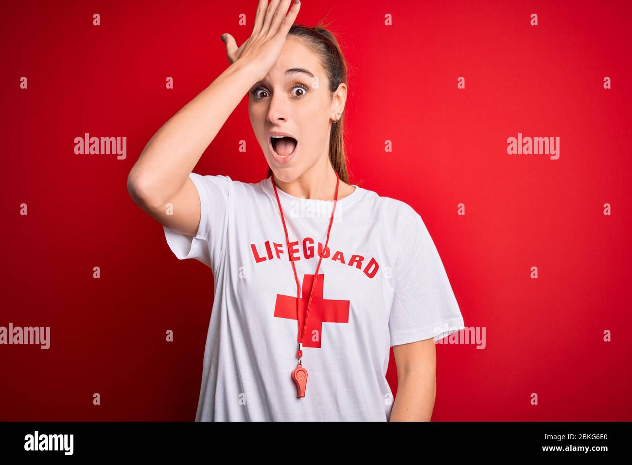 Beautiful lifeguard woman wearing t-shirt with red cross using whistle ...