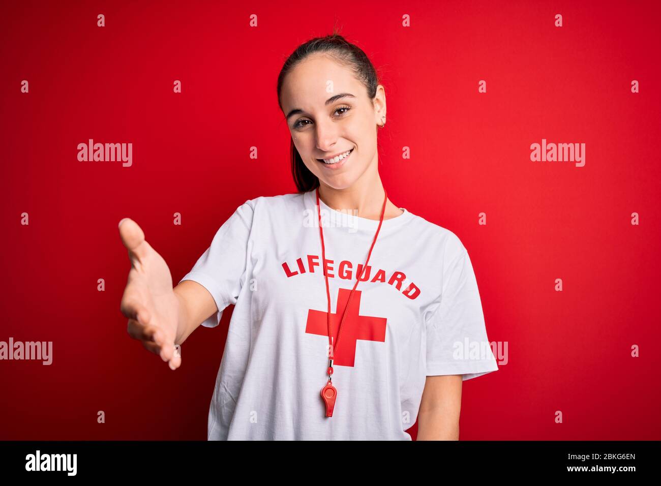 Beautiful lifeguard woman wearing t-shirt with red cross using whistle ...
