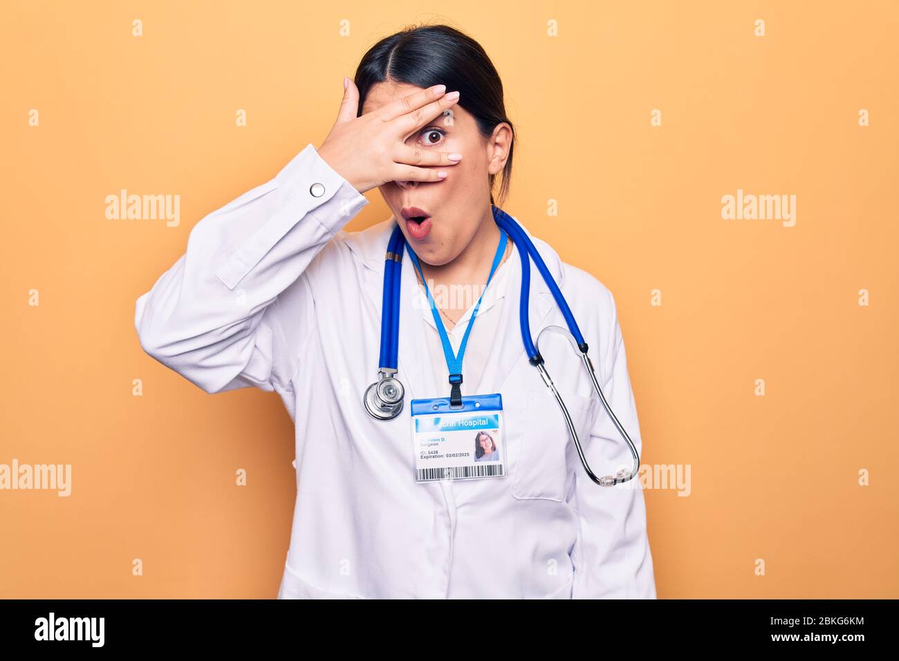 Young beautiful doctor woman wearing stethoscope and id card over isolated yellow background ...