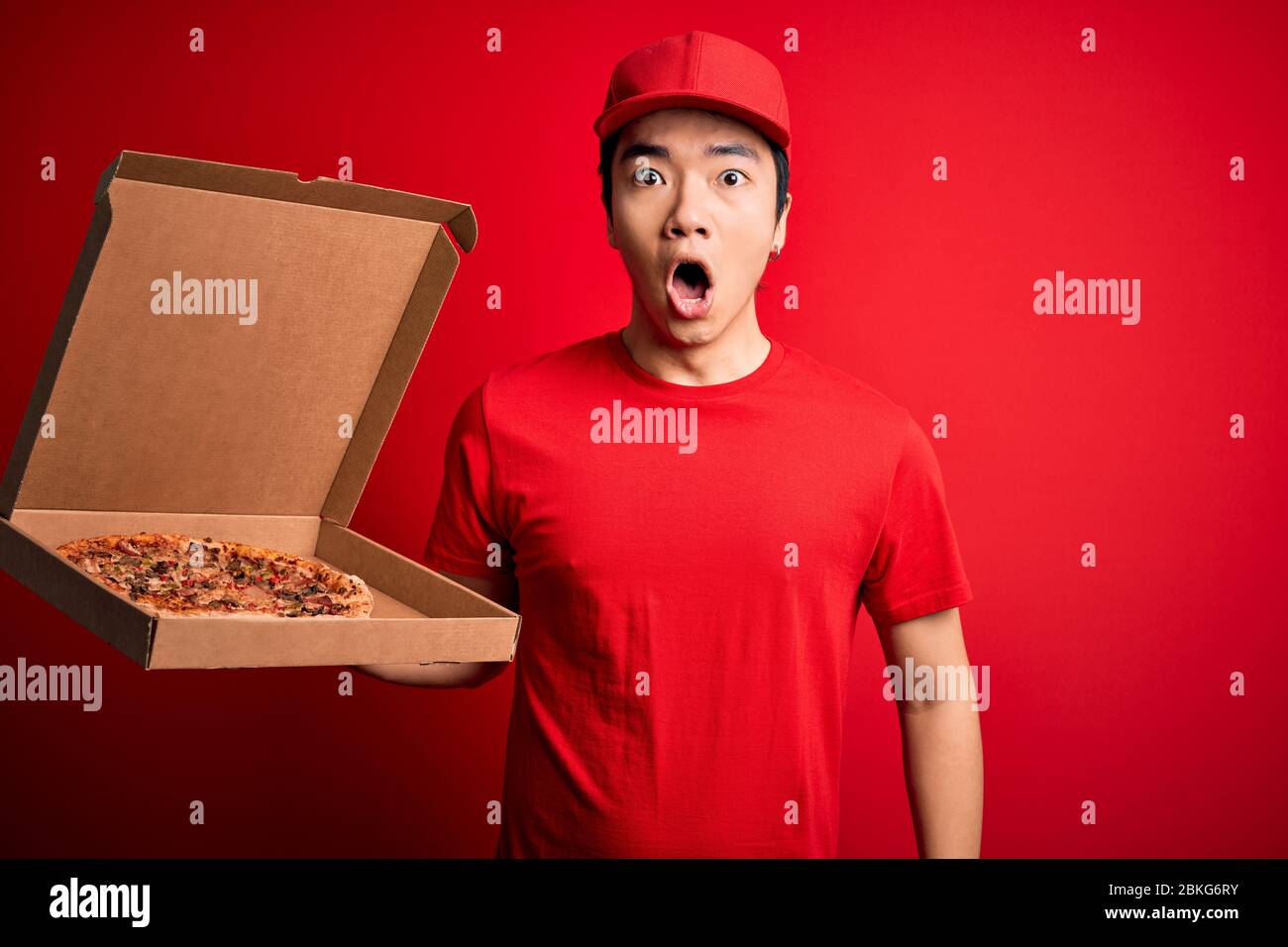 Young handsome chinese delivery man holding deliver box with delicious ...