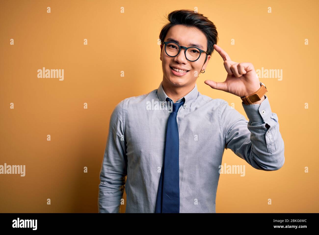 Young handsome chinese businessman wearing glasses and tie over yellow ...