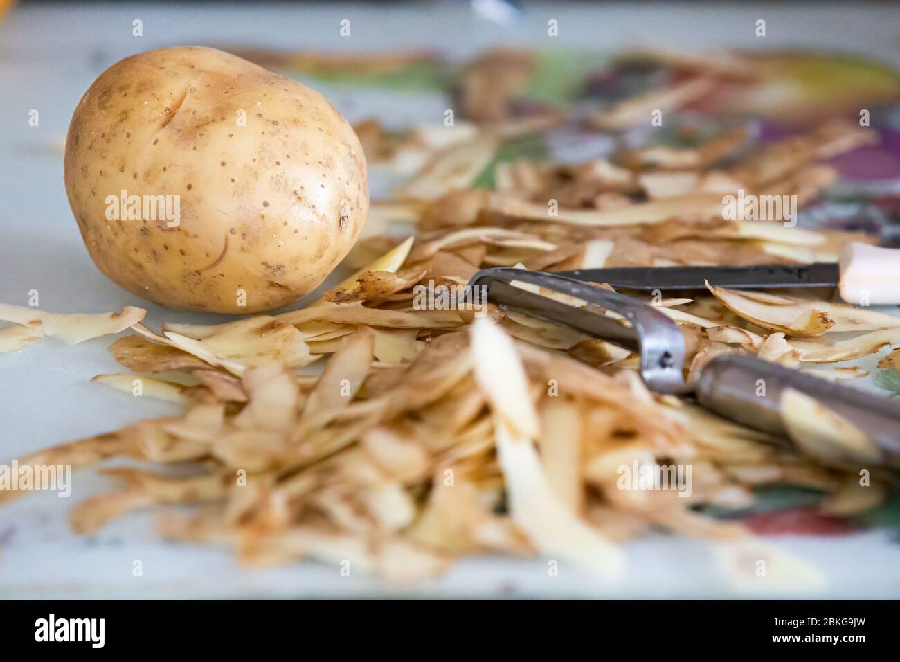 Potato and potato peelings with a potato peeler and knife and a glass ...