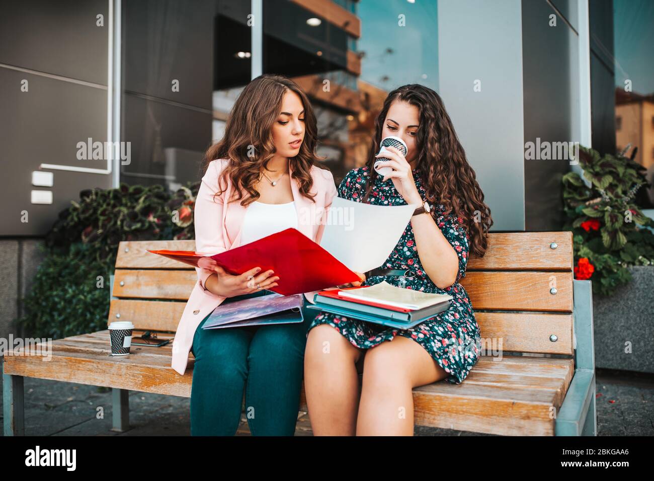 Two beautiful female friends, students checking paper notes and helping ...