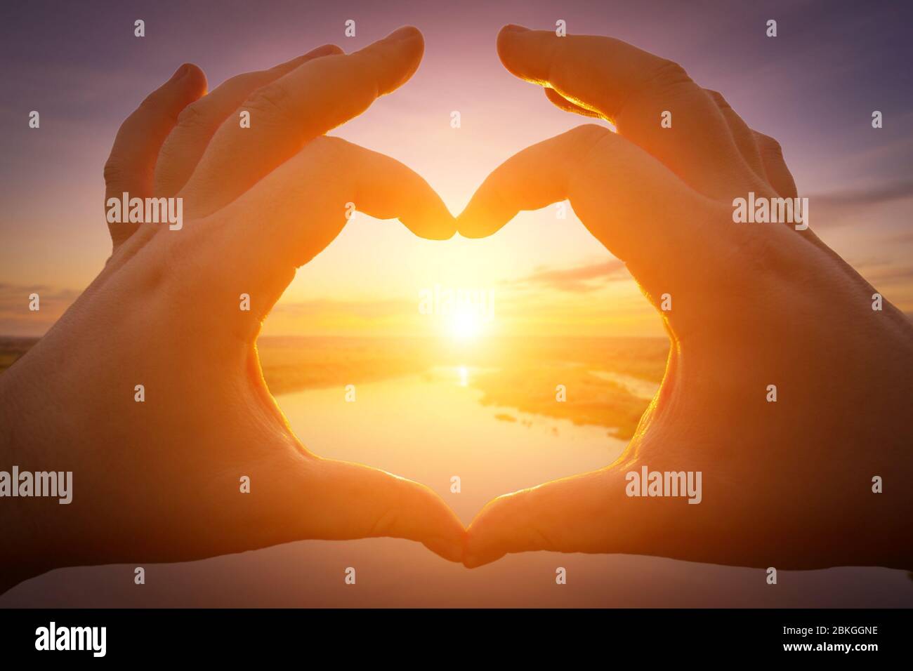 Hands in the shape of heart against the sunset or sunrise over the lake ...