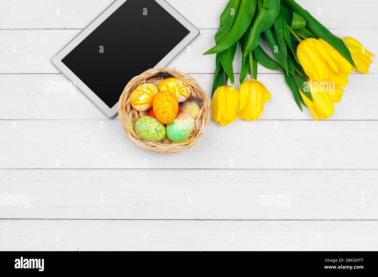 tablet screen for message and colorful tulips and easter eggs on wooden ...
