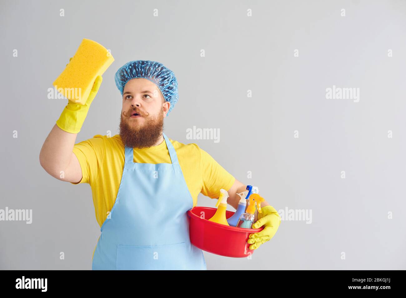 Funny fat man with a beard in an apron washing cleans up on a gray ...