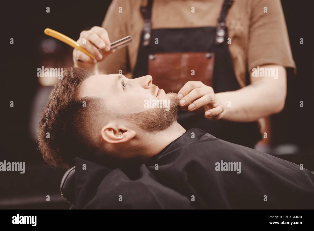 Barber cuts his beard to man in armchair Stock Photo - Alamy