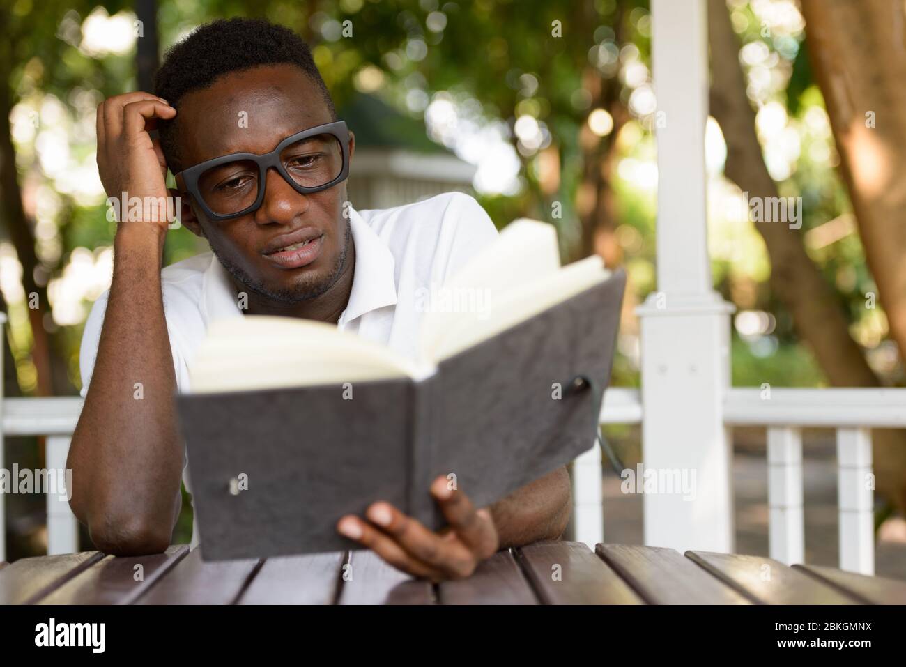 Stressed young African man as student reading book and scratching head ...