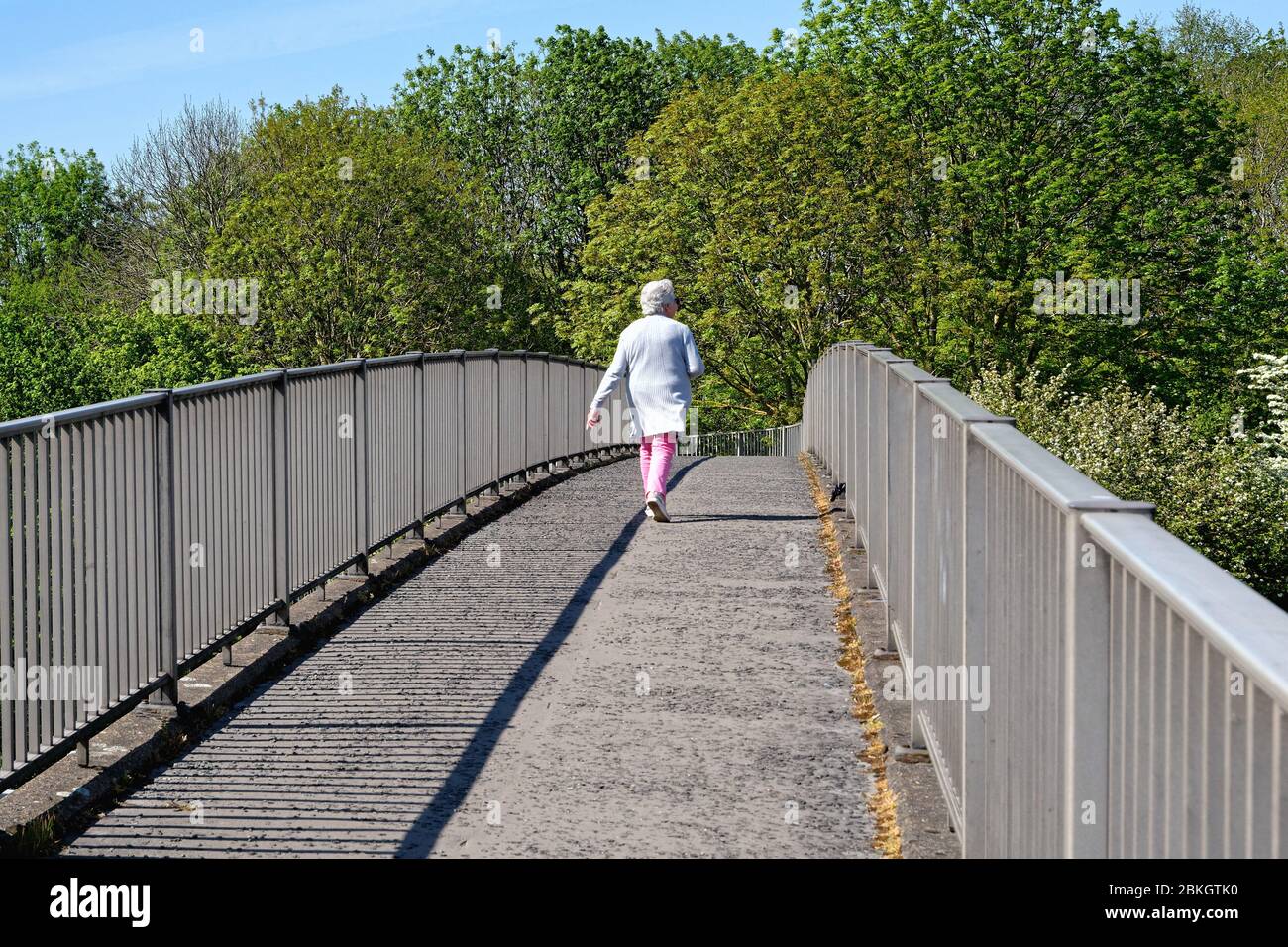 A rear view of an elderly lady walking across a pedestrian bridge over ...