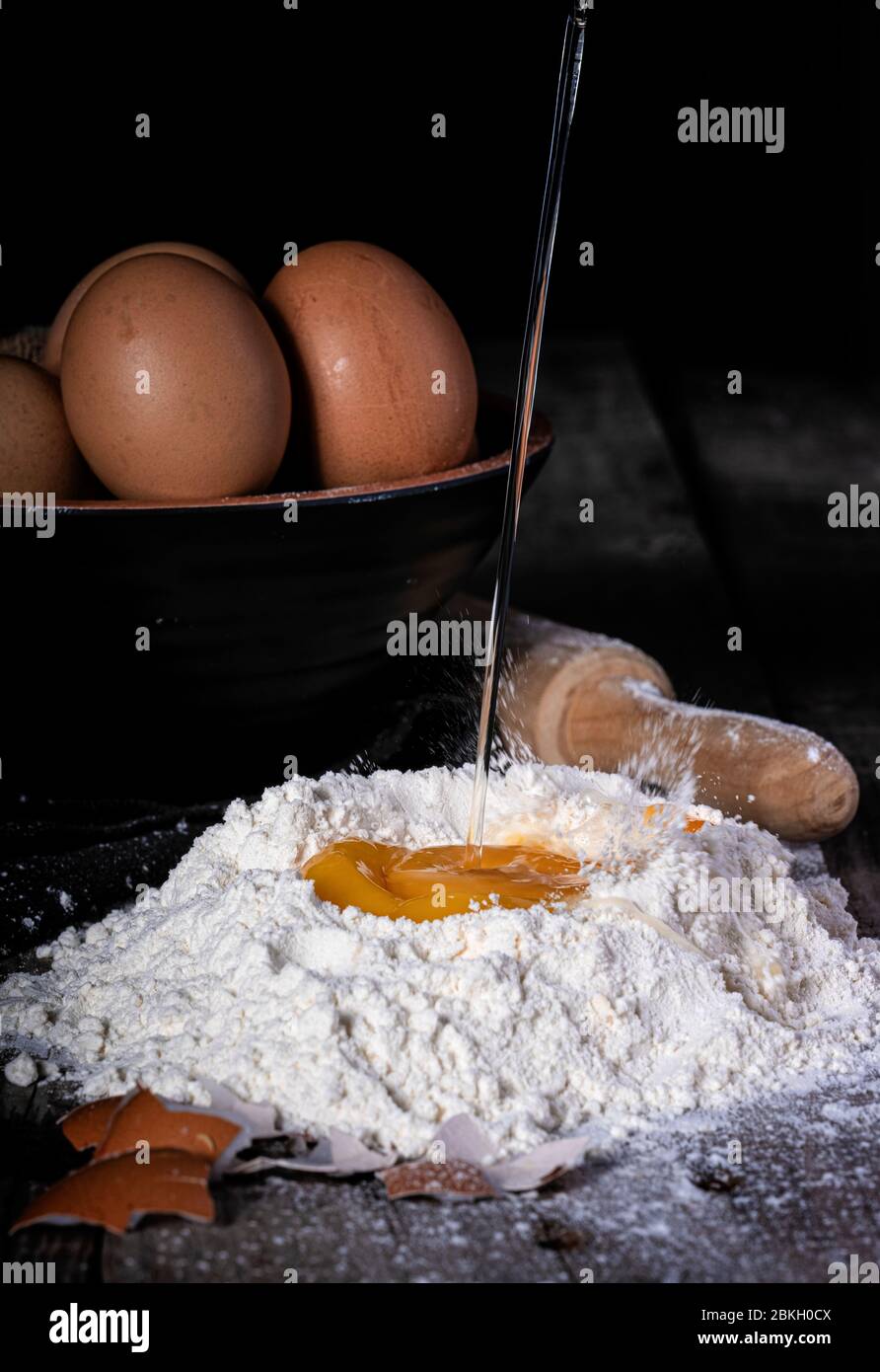 egg falling on flour, bottom bowl with eggs and wooden kneader Stock ...