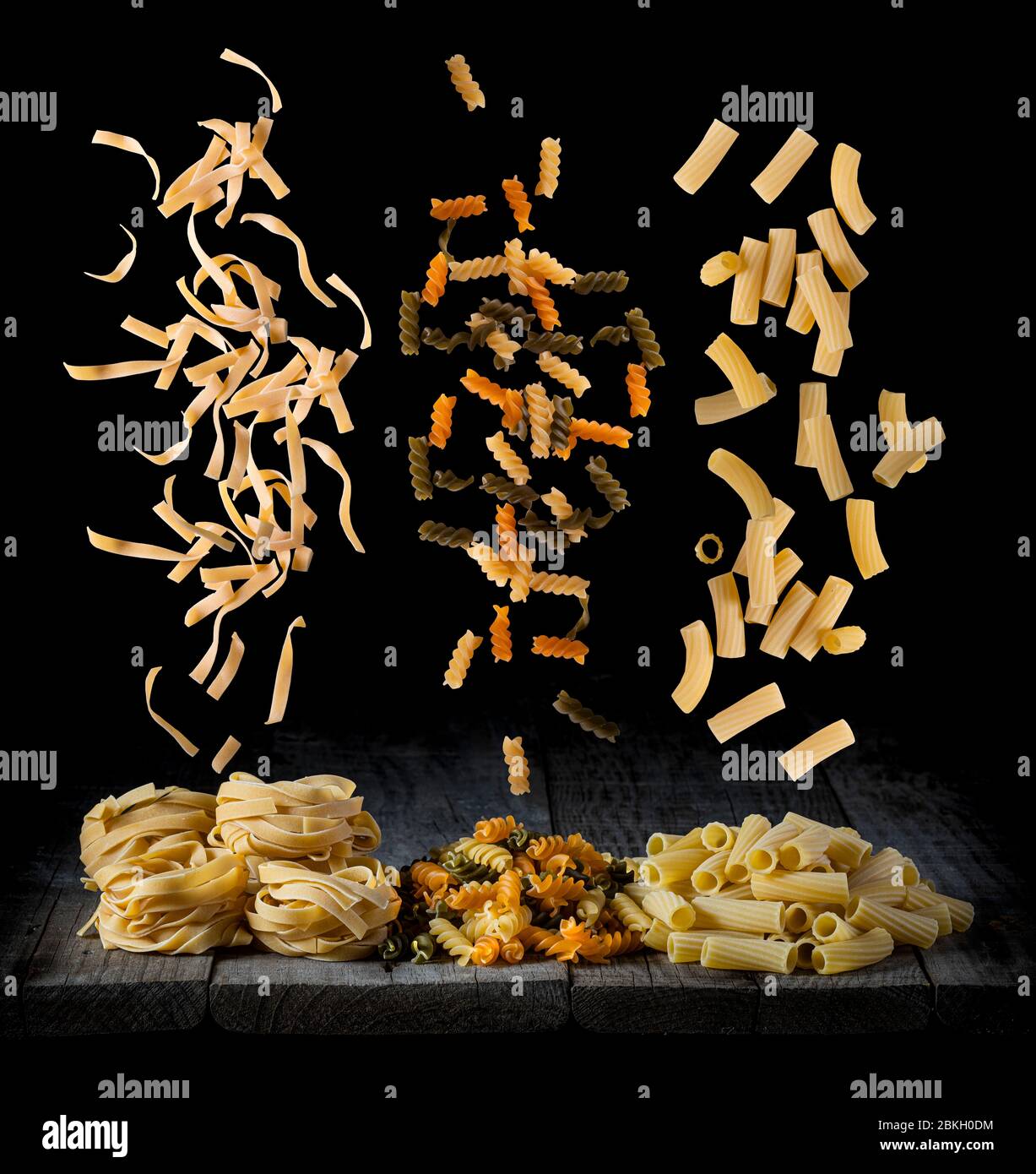 fresh pasta falling in different shapes and colours on a wood in front ...