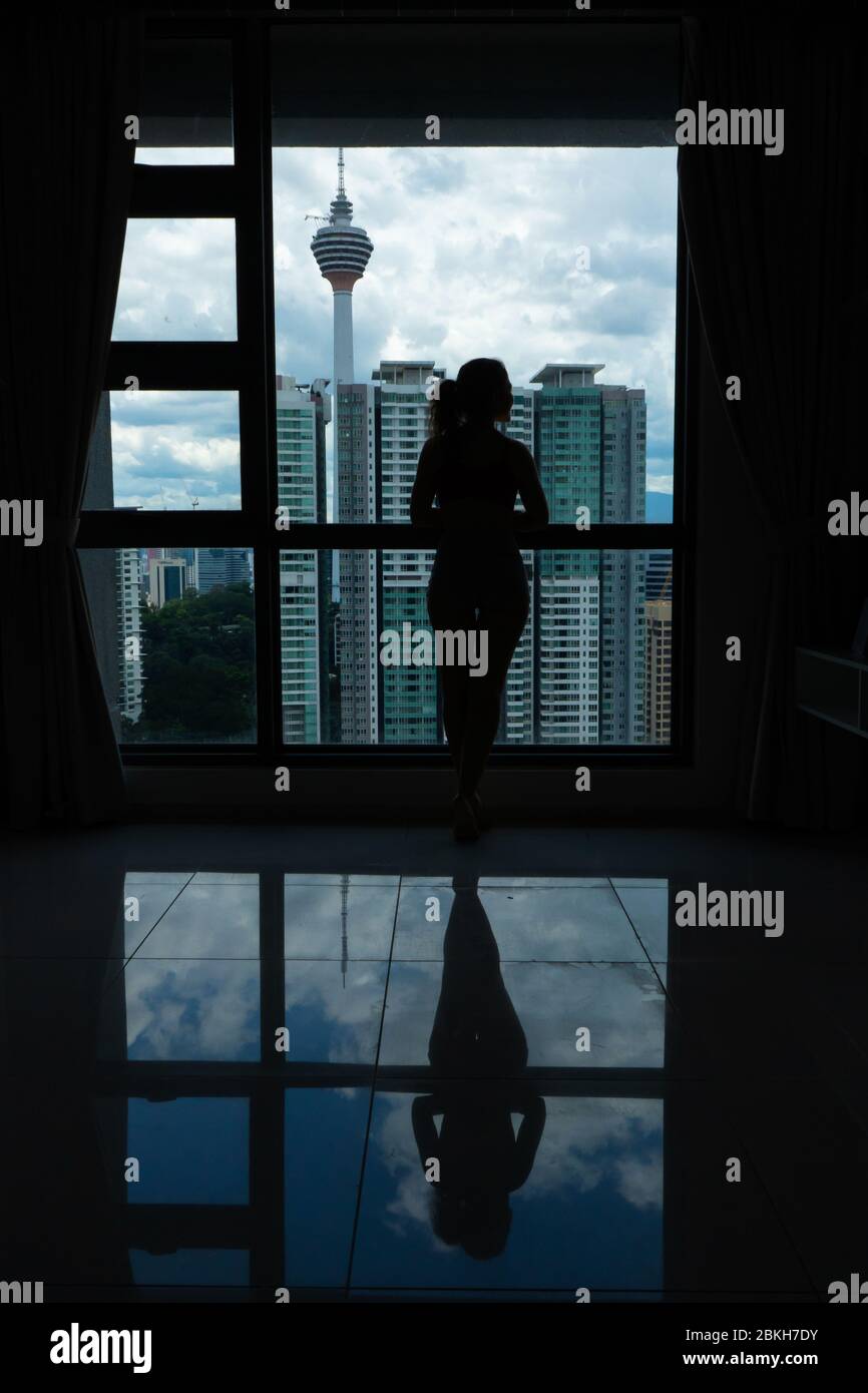 A slender girl is looking at the city through a large window. High ...