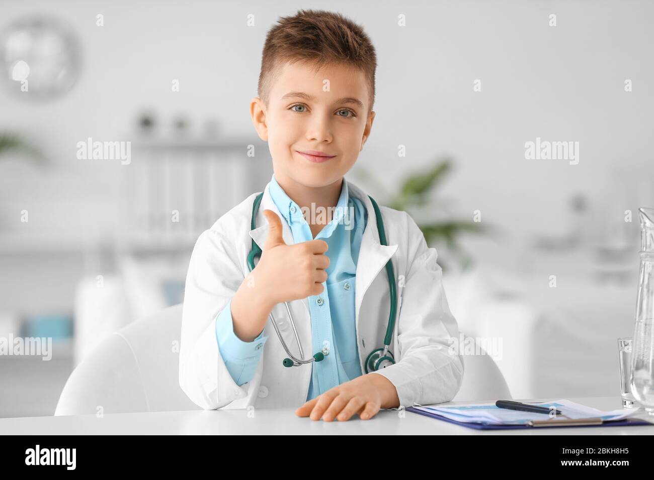 Cute little doctor showing thumb-up gesture in clinic Stock Photo - Alamy
